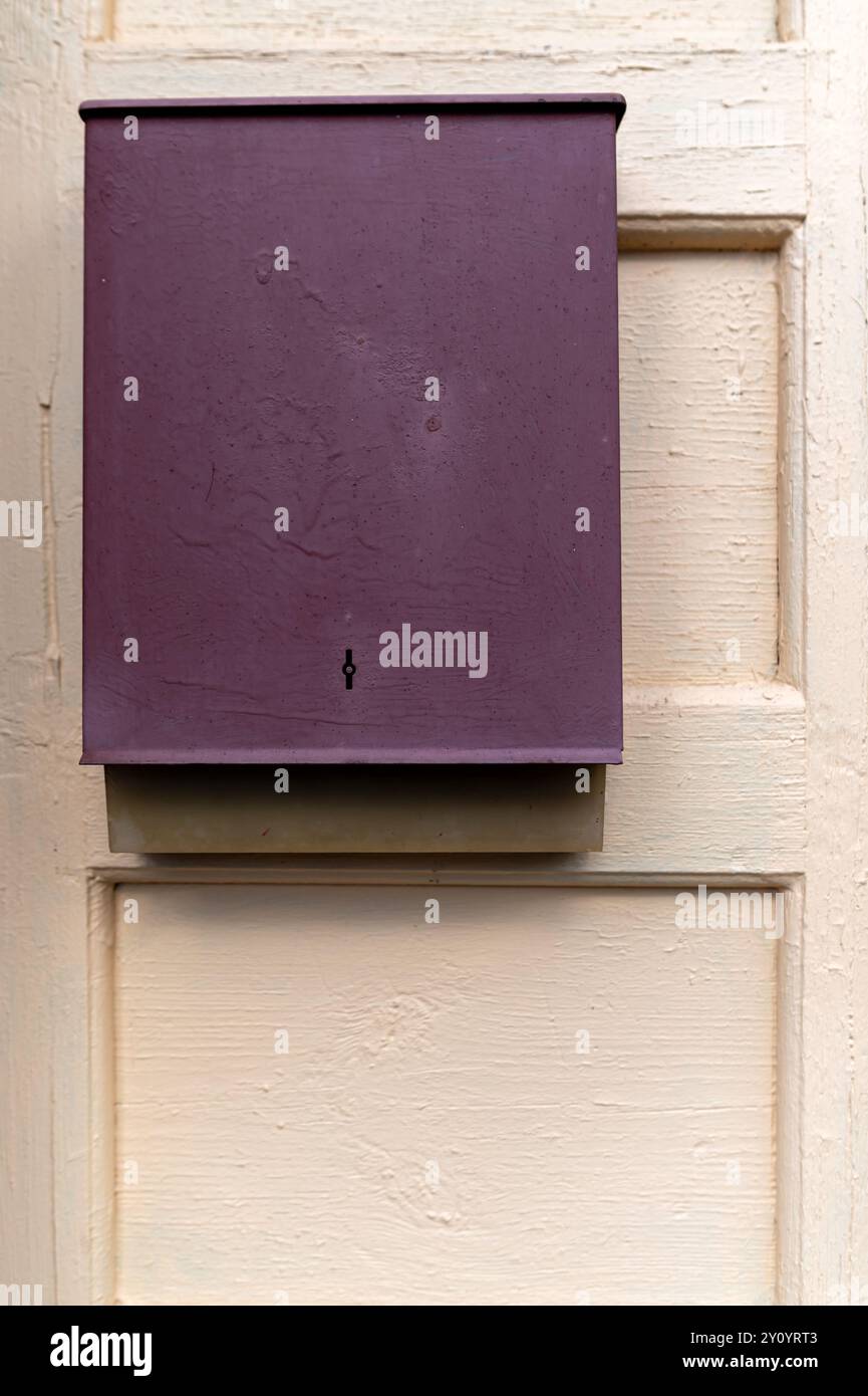 A purple mailbox is attached to a light-colored wooden door, reflecting ...