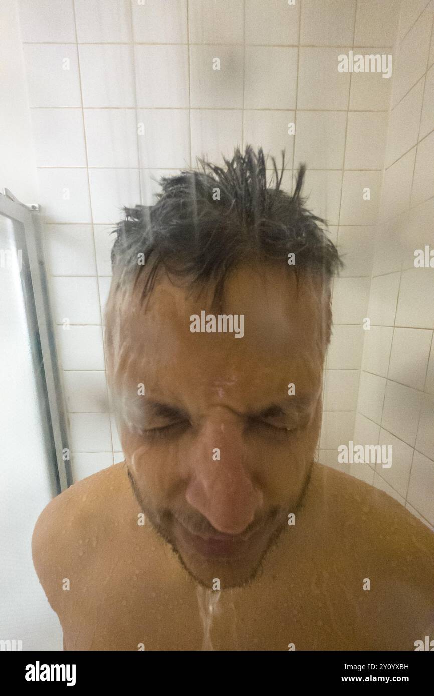 A man is standing in a shower with water pouring down his face. He is ...