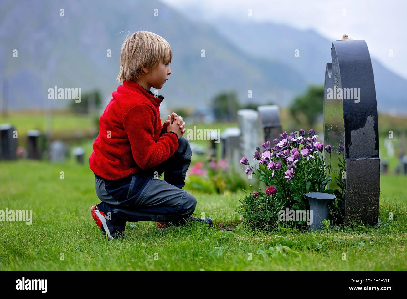 Sad little child, blond boy, standing in the rain on cemetery, sad ...