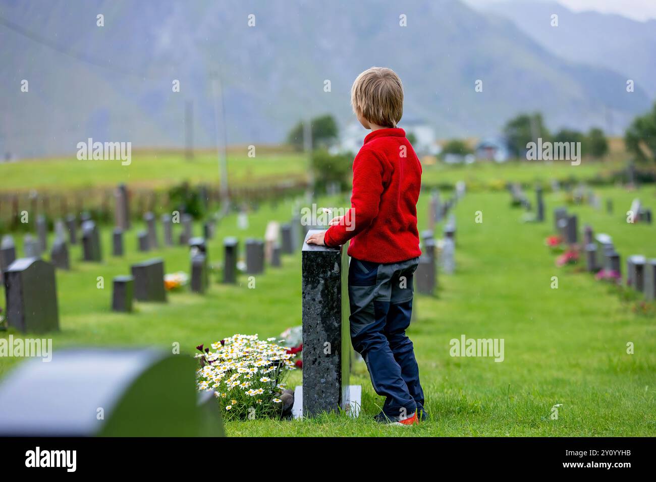 Sad little child, blond boy, standing in the rain on cemetery, sad ...