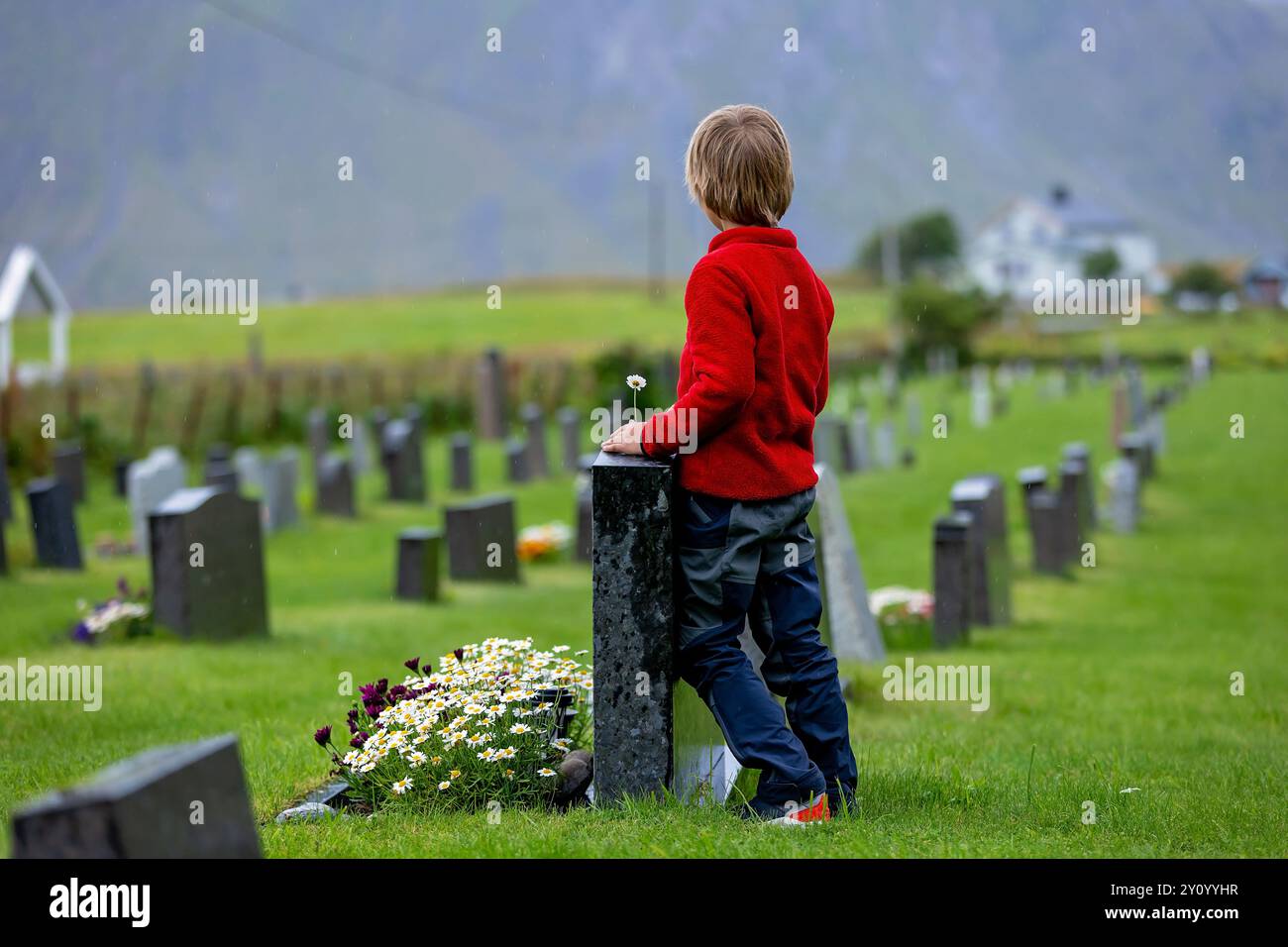 Sad little child, blond boy, standing in the rain on cemetery, sad ...