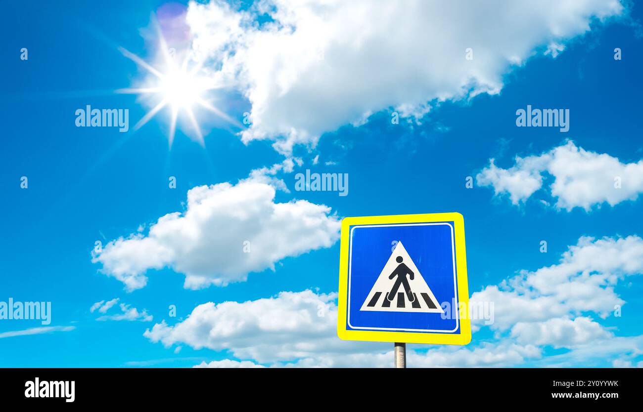A pedestrian crossing sign set against a bright blue sky with fluffy ...