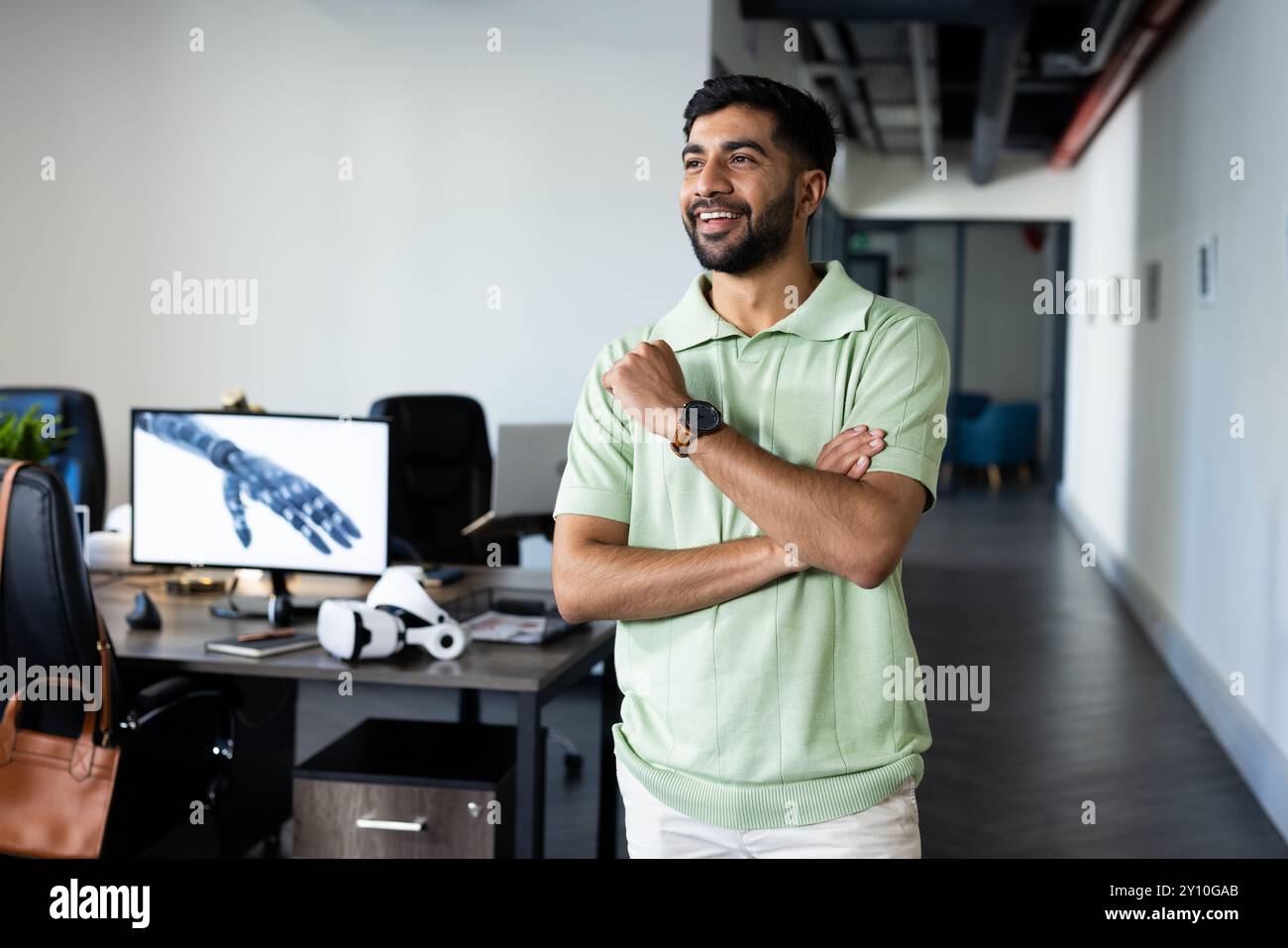 Smiling Indian man in office with robotic arm on computer screen in ...