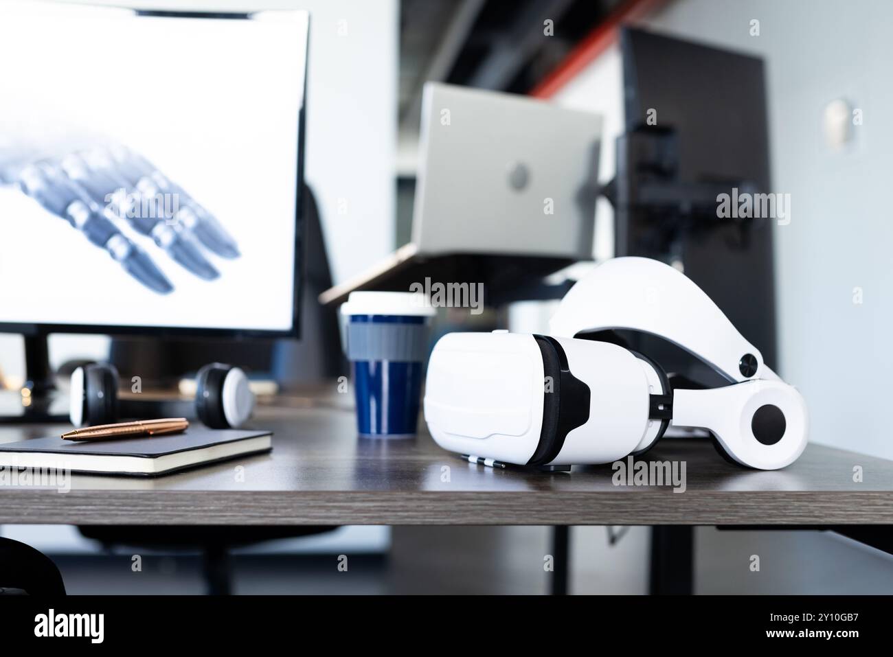 VR headset and robotic arm on desk with laptop and coffee cup in office ...