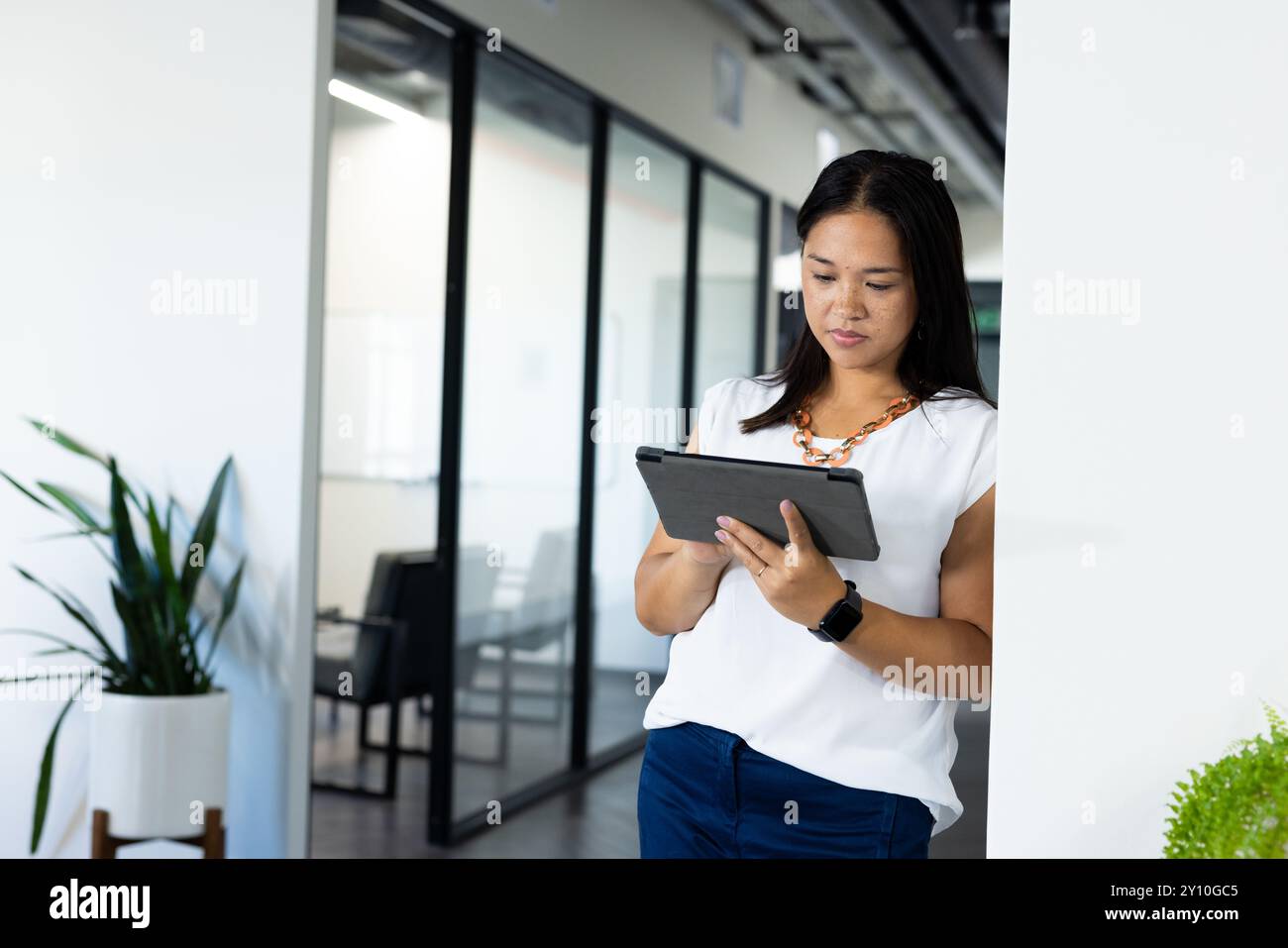 Using tablet, woman standing in modern office, focusing on work tasks ...