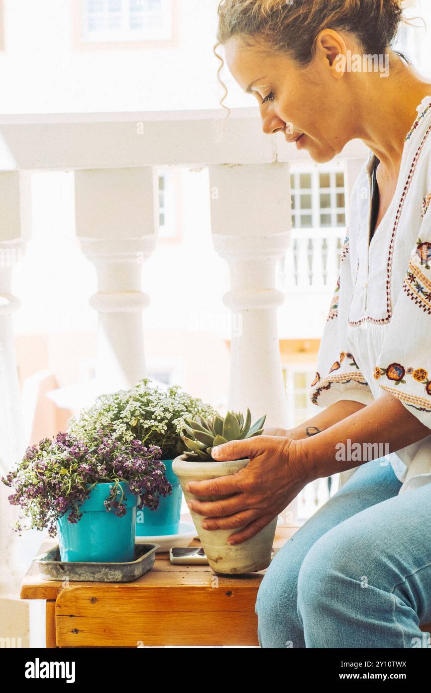 Beautiful lady takes care of her plants on the balcony. Sitting blonde ...