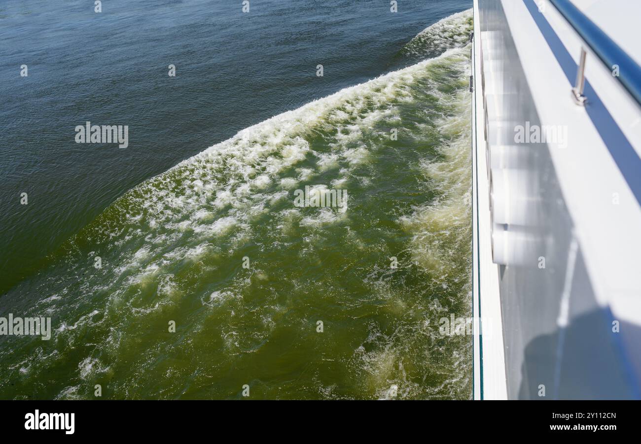 Foamy wake of ship's propeller churning green river water, viewed from ...