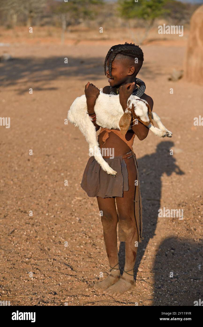 Limba girl holding a young goat in her arms, Kunene, Kaokoveld, Namibia ...