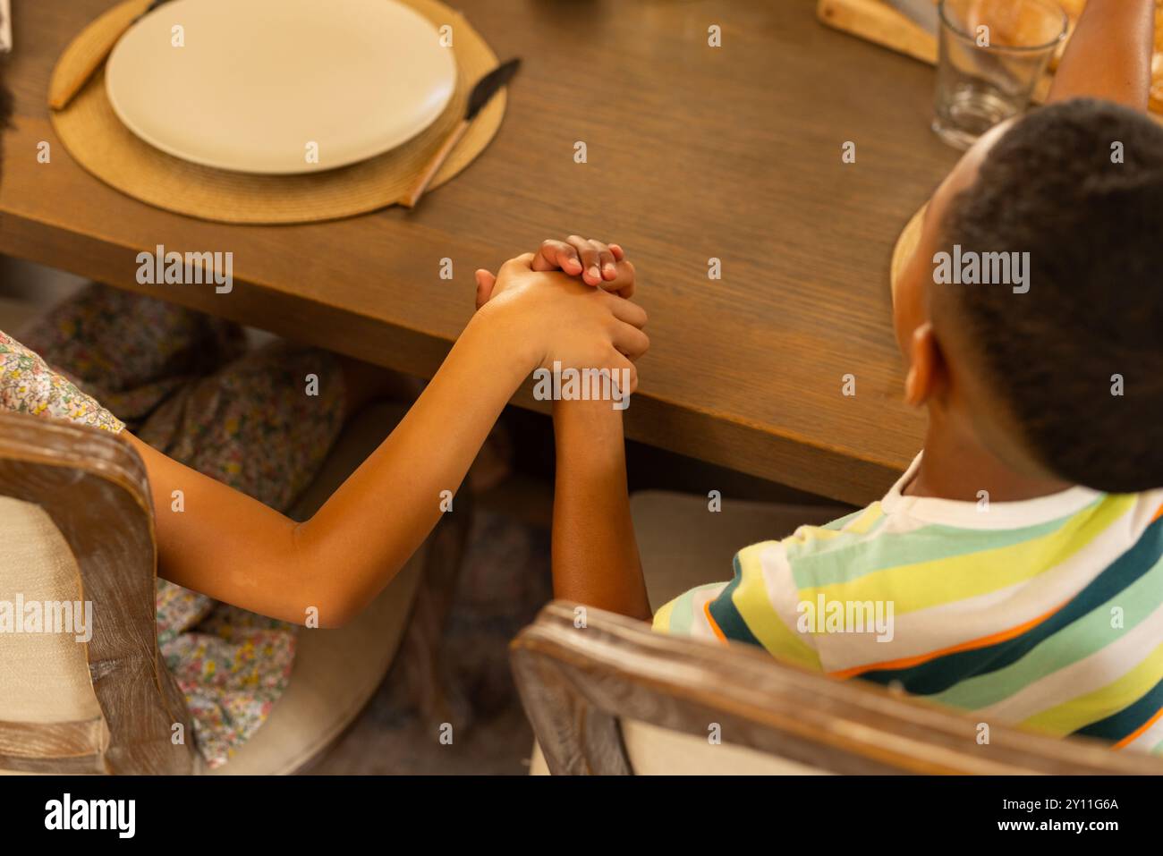 Holding hands, children sitting at dining table with plates and cutlery ...