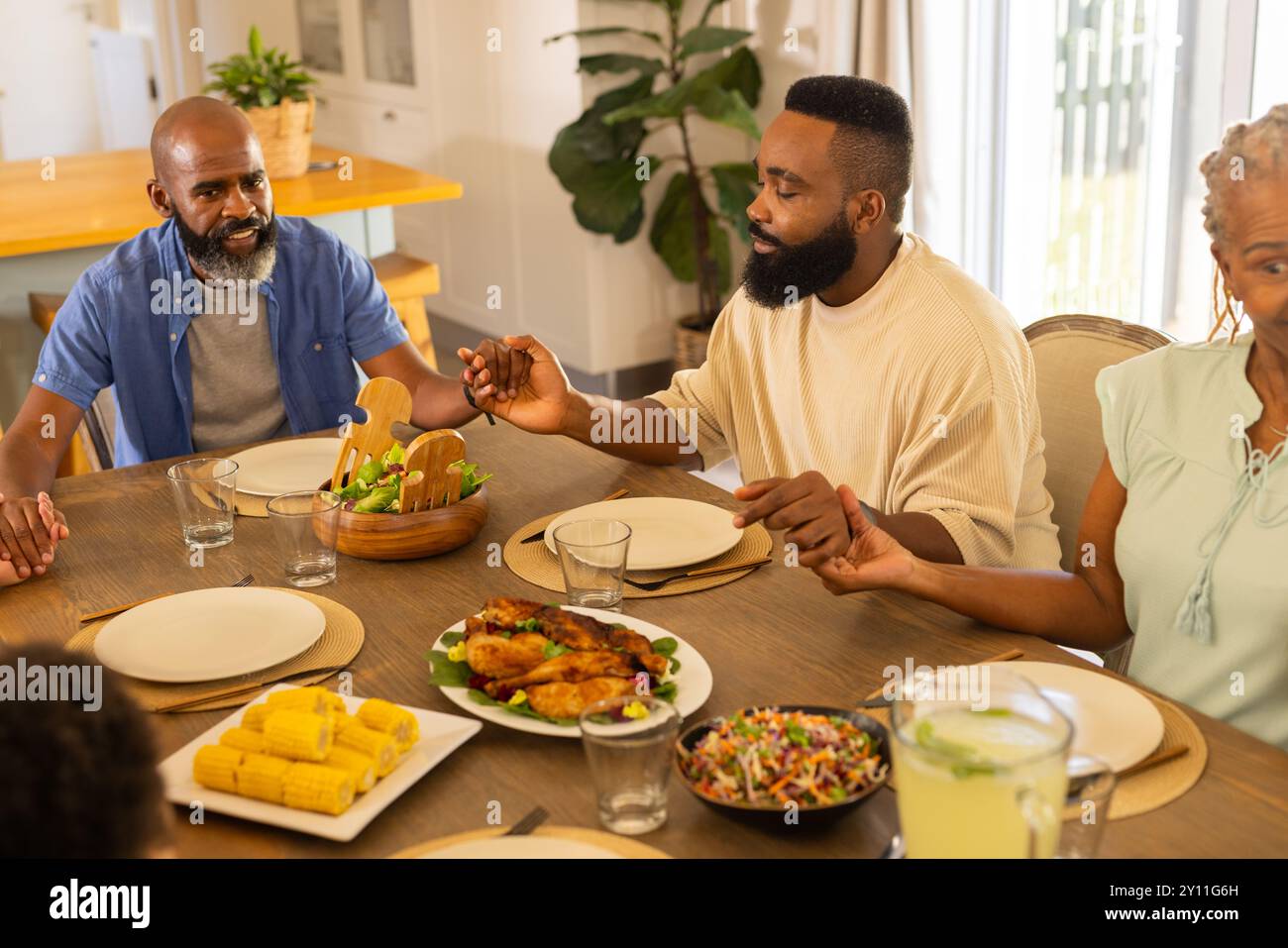 multigenerational family holding hands and praying before meal ...