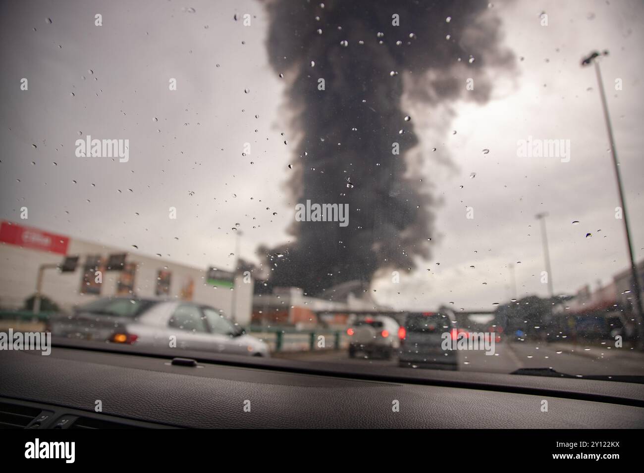 Through a rain-speckled windshield, a massive column of black smoke ...