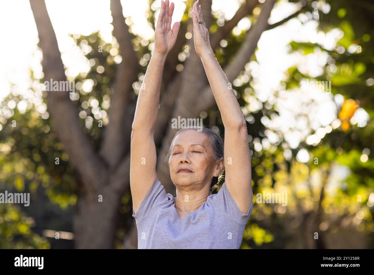 Practicing yoga outdoors, senior asian woman raising arms and closing ...