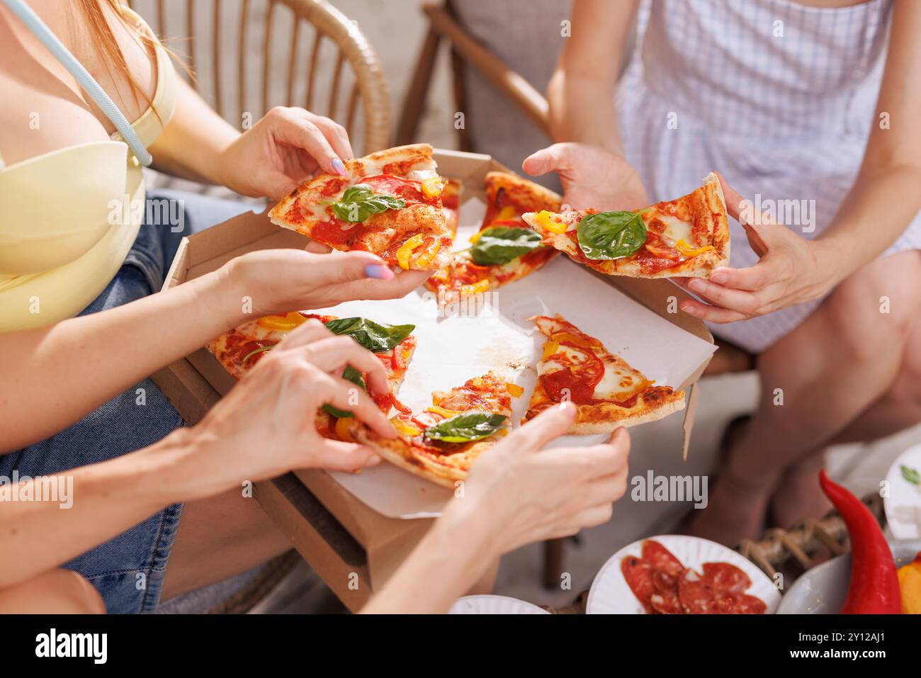 A group of friends share pizza outdoors, hands reaching for slices ...