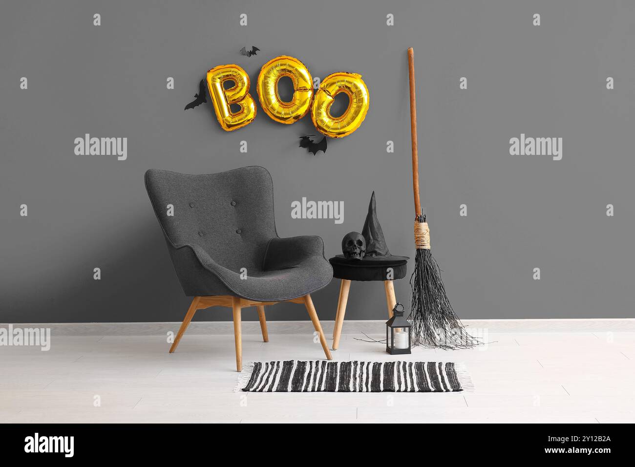 Armchair, witch broom and text BOO made of balloons hanging on grey ...