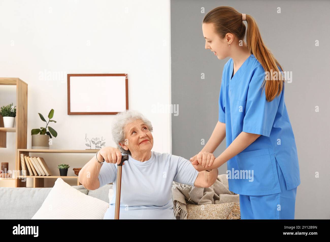 Female caregiver helping senior woman to stand up at home Stock Photo ...
