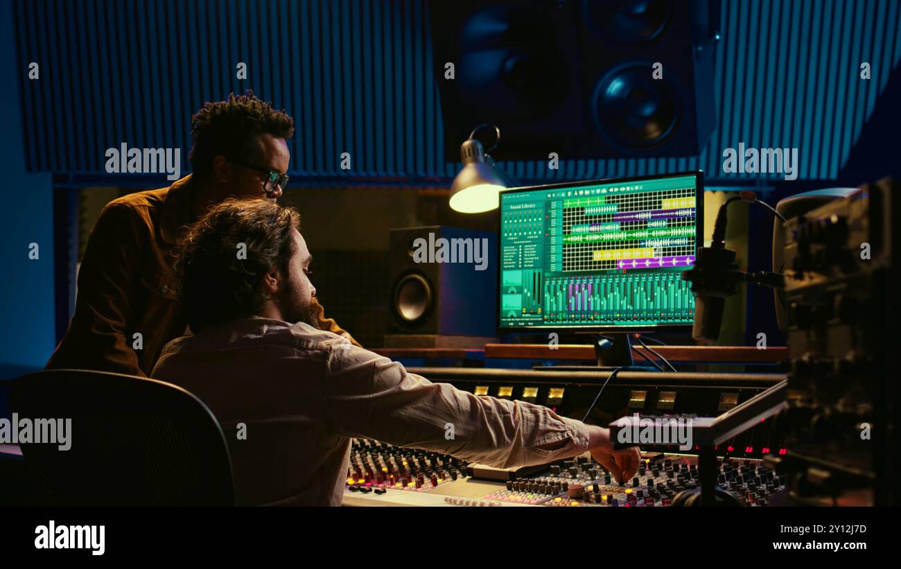Musician and producer work on soundboard pads at professional studio ...
