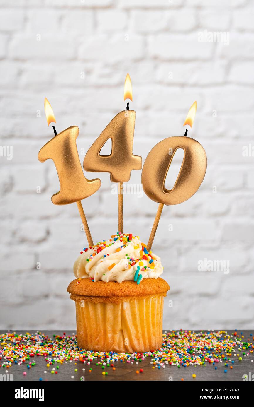 Cupcake with number 140 birthday candle - White block wall background Stock Photo - Alamy
