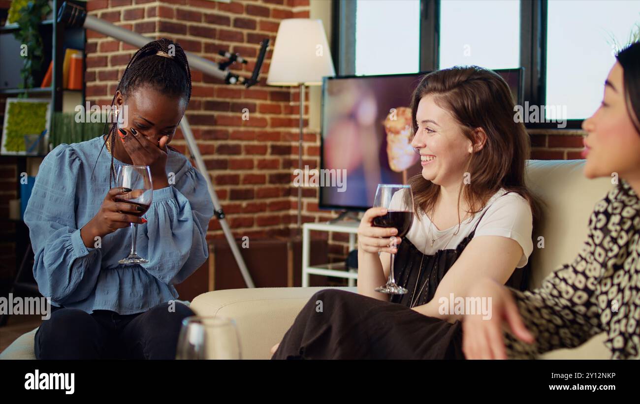 BFFs talking on couch, drinking alcohol beverages at friends social ...