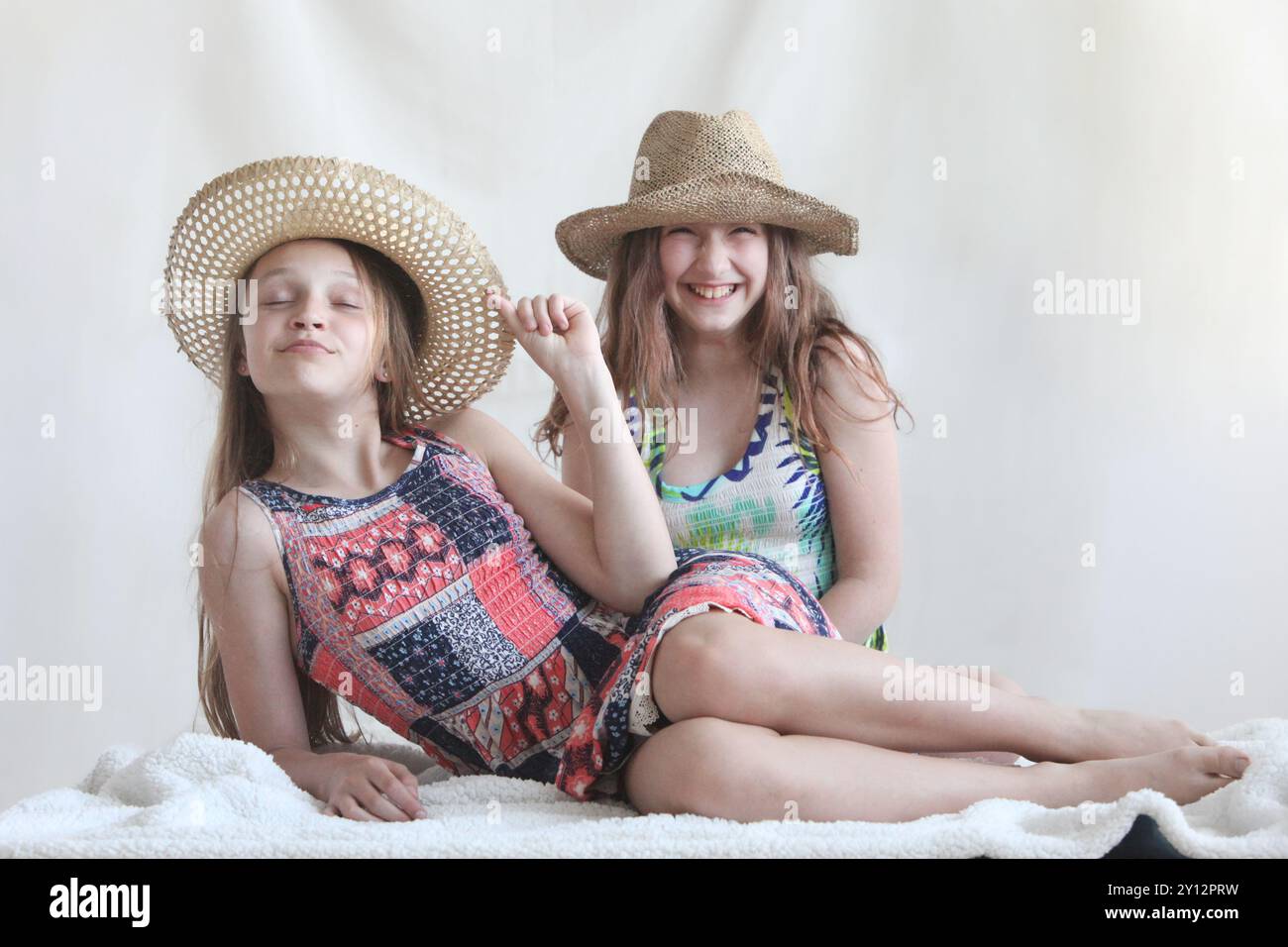 portrait of two happy preteen girls in sundresses and straw hats ...