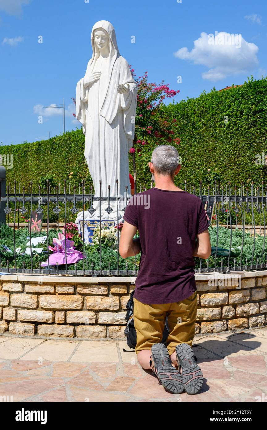 People praying around the statue of the Queen of Peace near the St ...