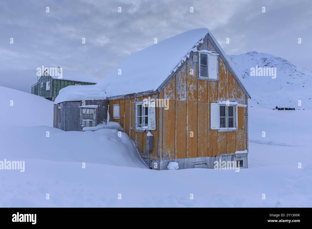 Typical Greenlandic house in deep snow in front of mountains, winter ...