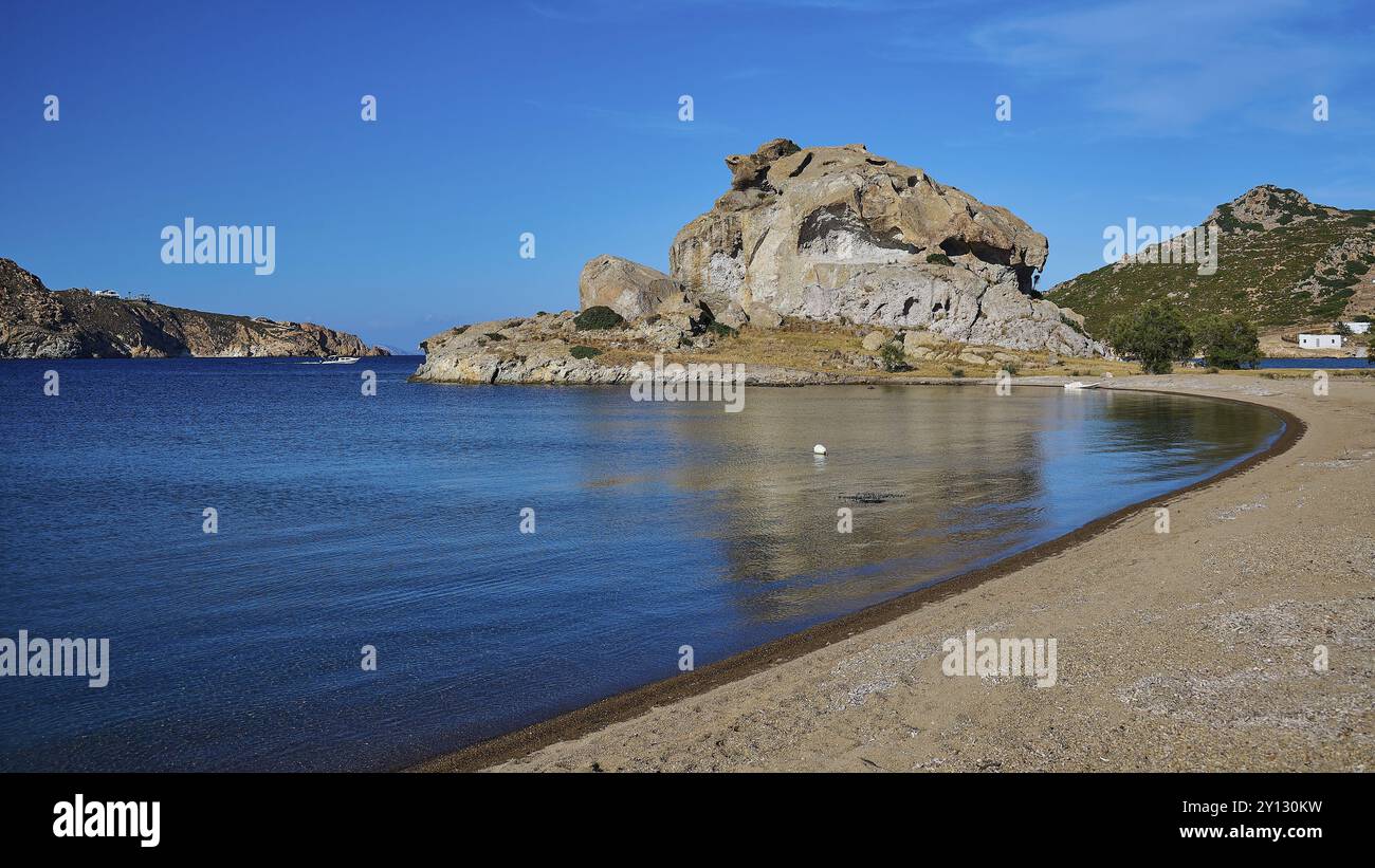 A quiet beach with a rock formation and calm waters under a clear blue ...