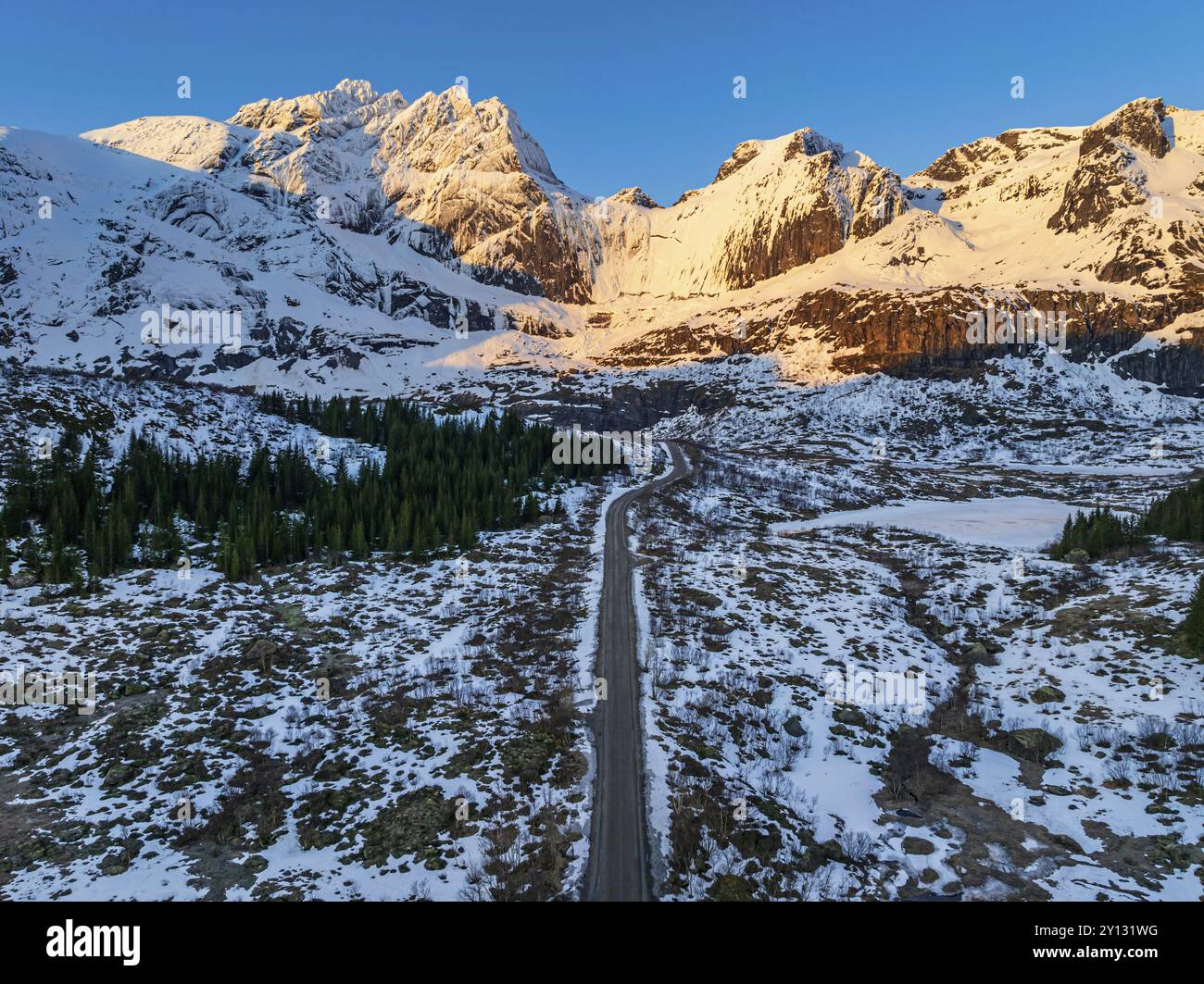 Aerial view of road in front of steep mountains, winter, sunrise ...
