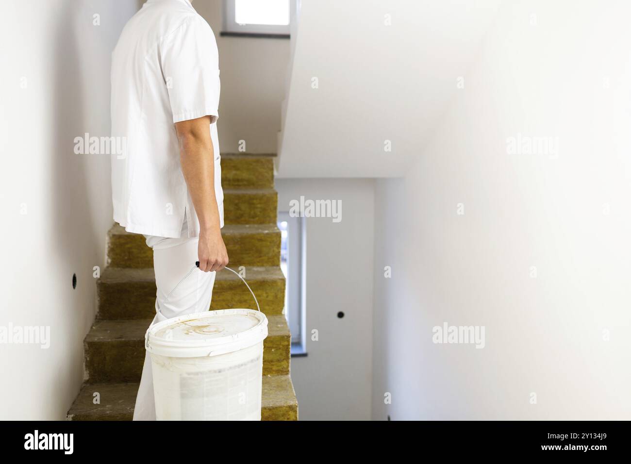 Painter man at work with a bucket of white paint standing at house ...