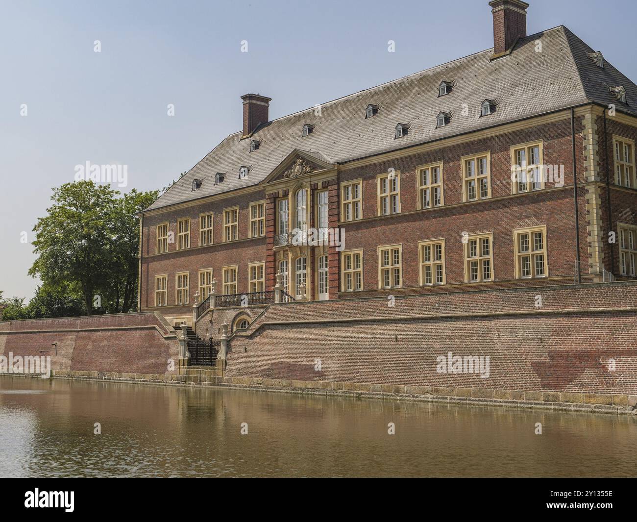 An impressive historic brick castle with many windows, next to a moat ...