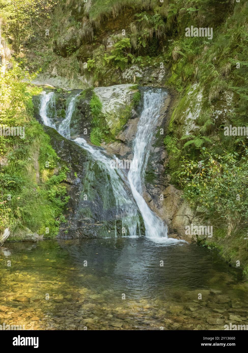 A multi-levelled waterfall flowing over moss-covered rocks into a clear ...
