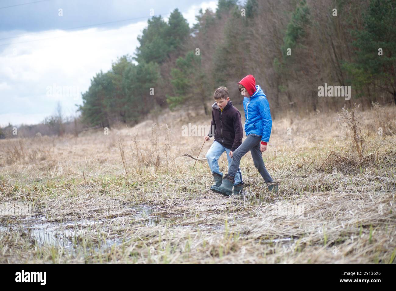 Two children explore a muddy field in early spring, collecting sticks ...