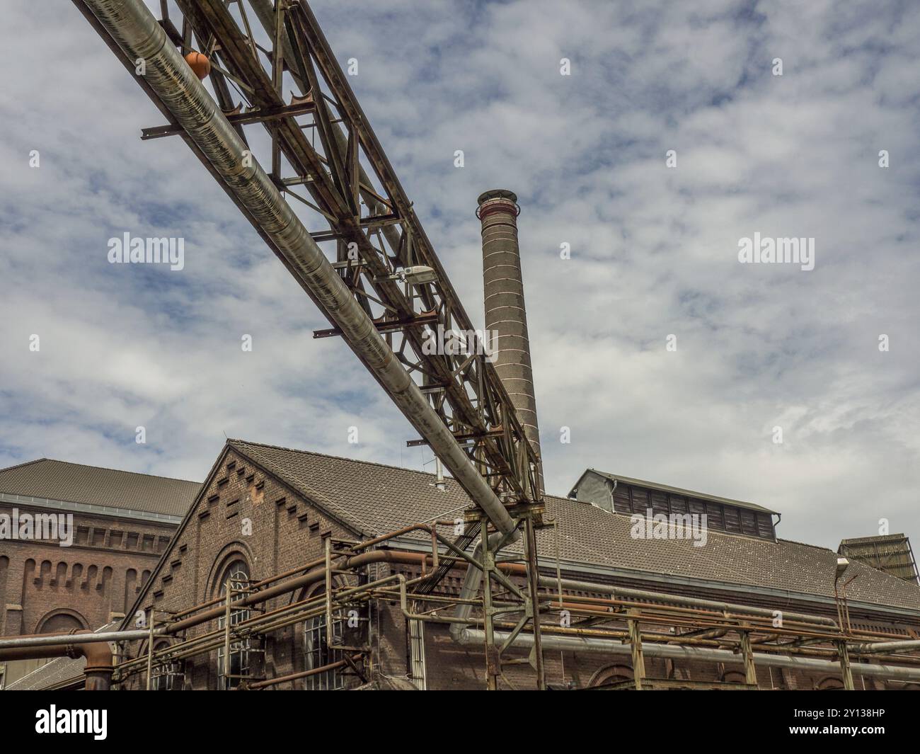 Historic factory building with chimney and steel girders under a cloudy ...