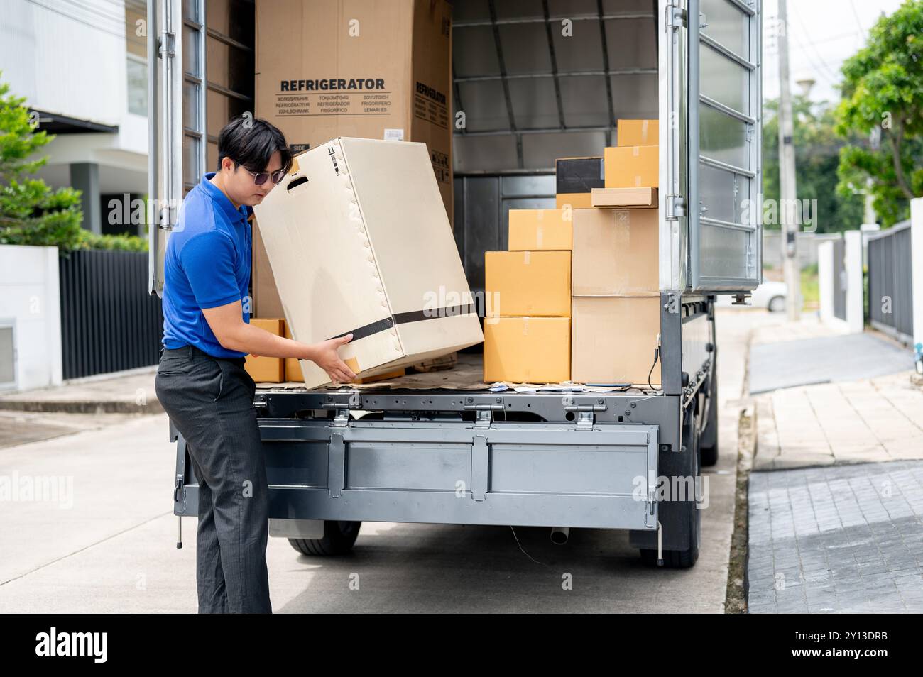 An Asian delivery man or mover in a blue uniform is unloading cardboard ...