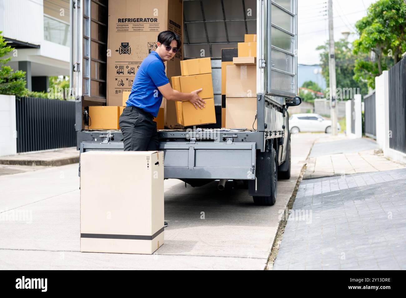 An Asian delivery man or mover in a blue uniform is unloading cardboard ...