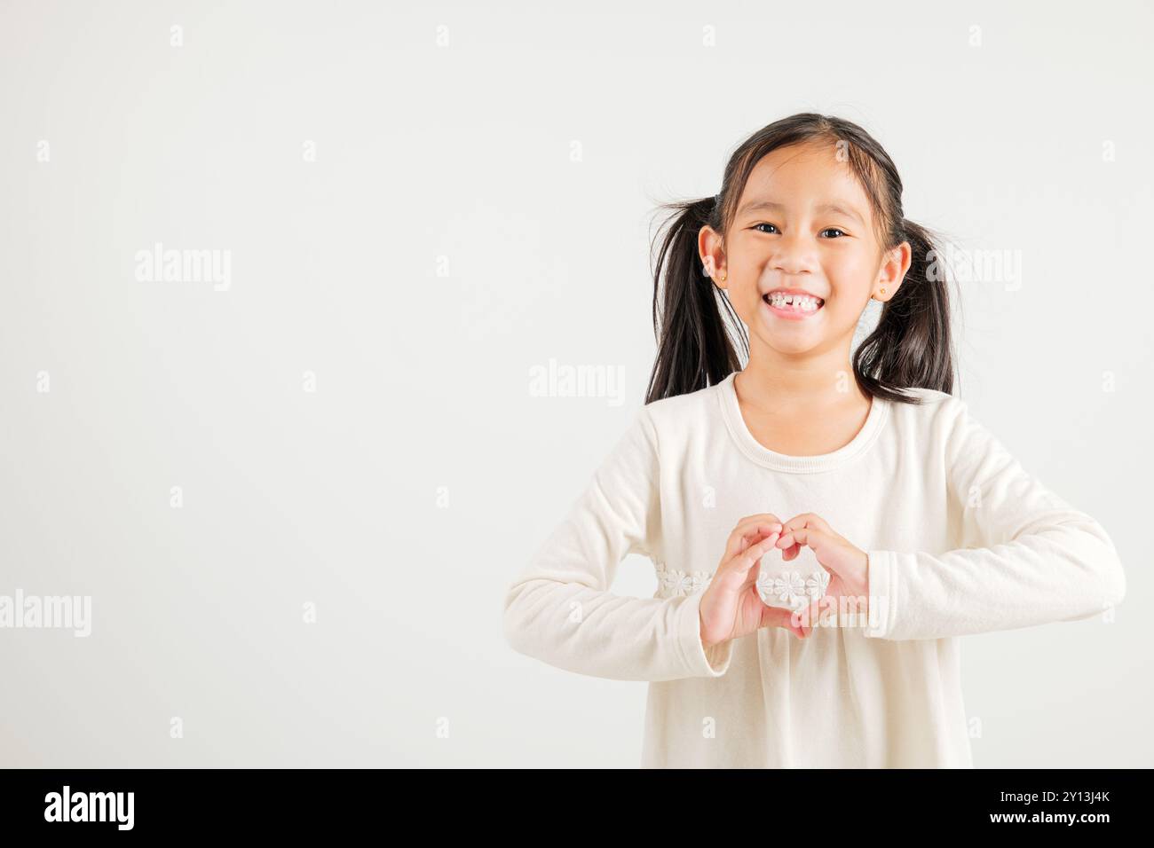 A smiling Asian young kid girl shows confidence, creating a heart shape ...