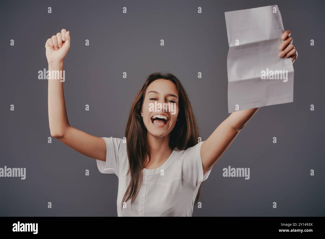 Young woman is joyfully raising her arms in the air, holding a piece of ...