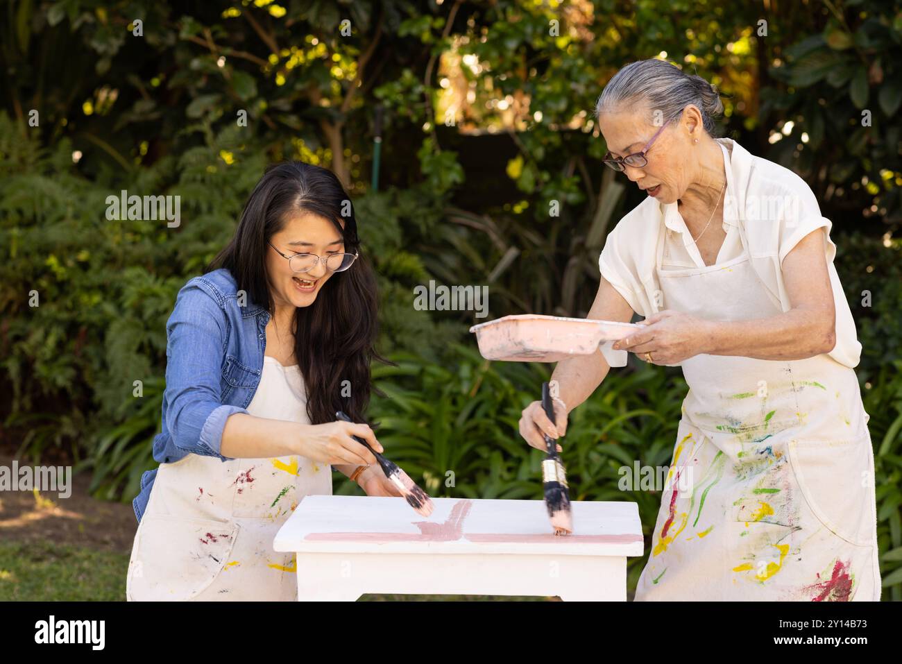 Painting table, asian granddaughter and grandmother enjoying outdoor diy project together in ...