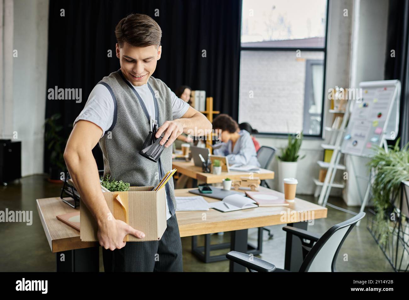 Young delighted man packing his items during lay off, colleagues on ...