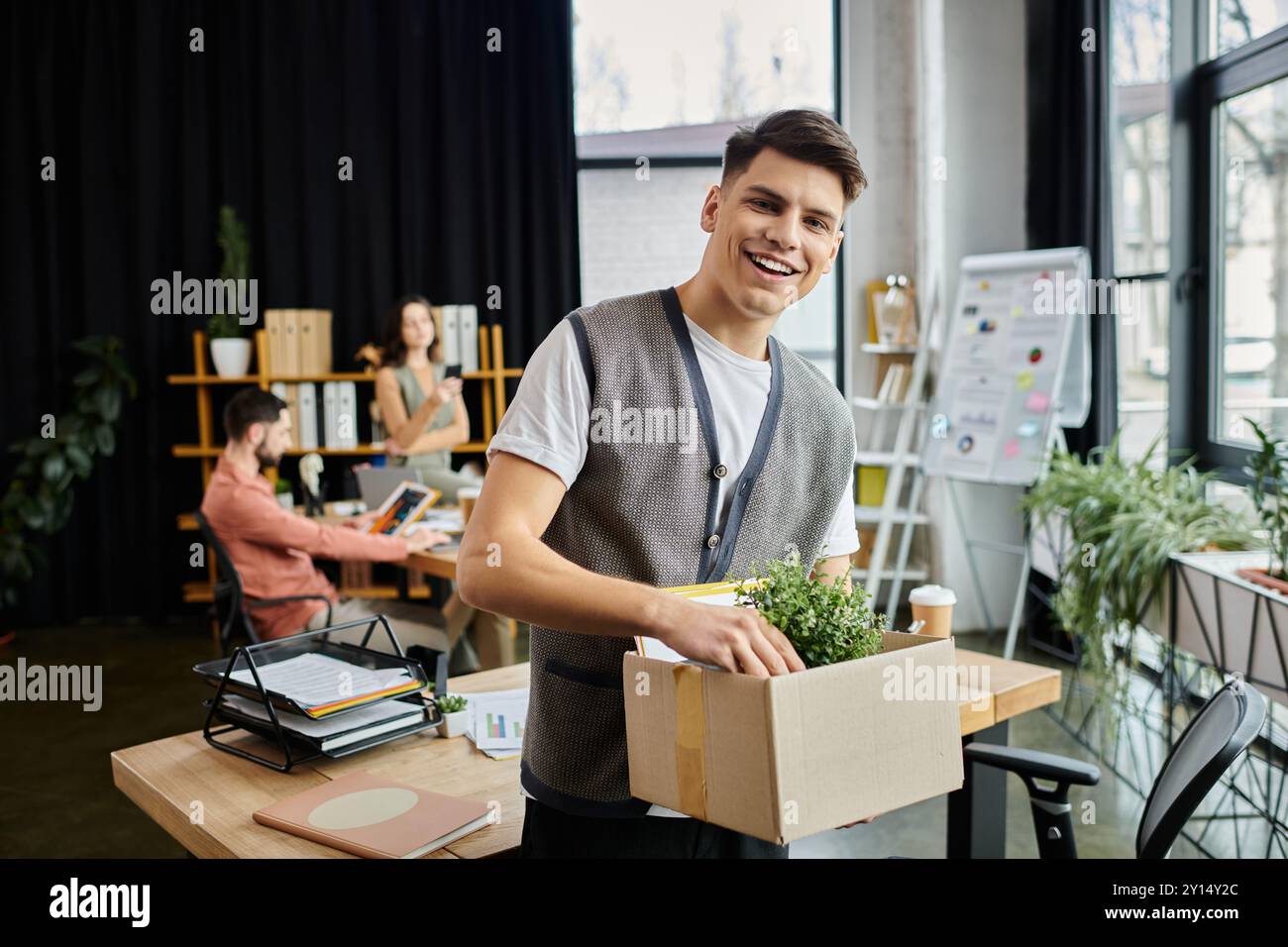 Young cheerful man packing his items during lay off, colleagues on ...