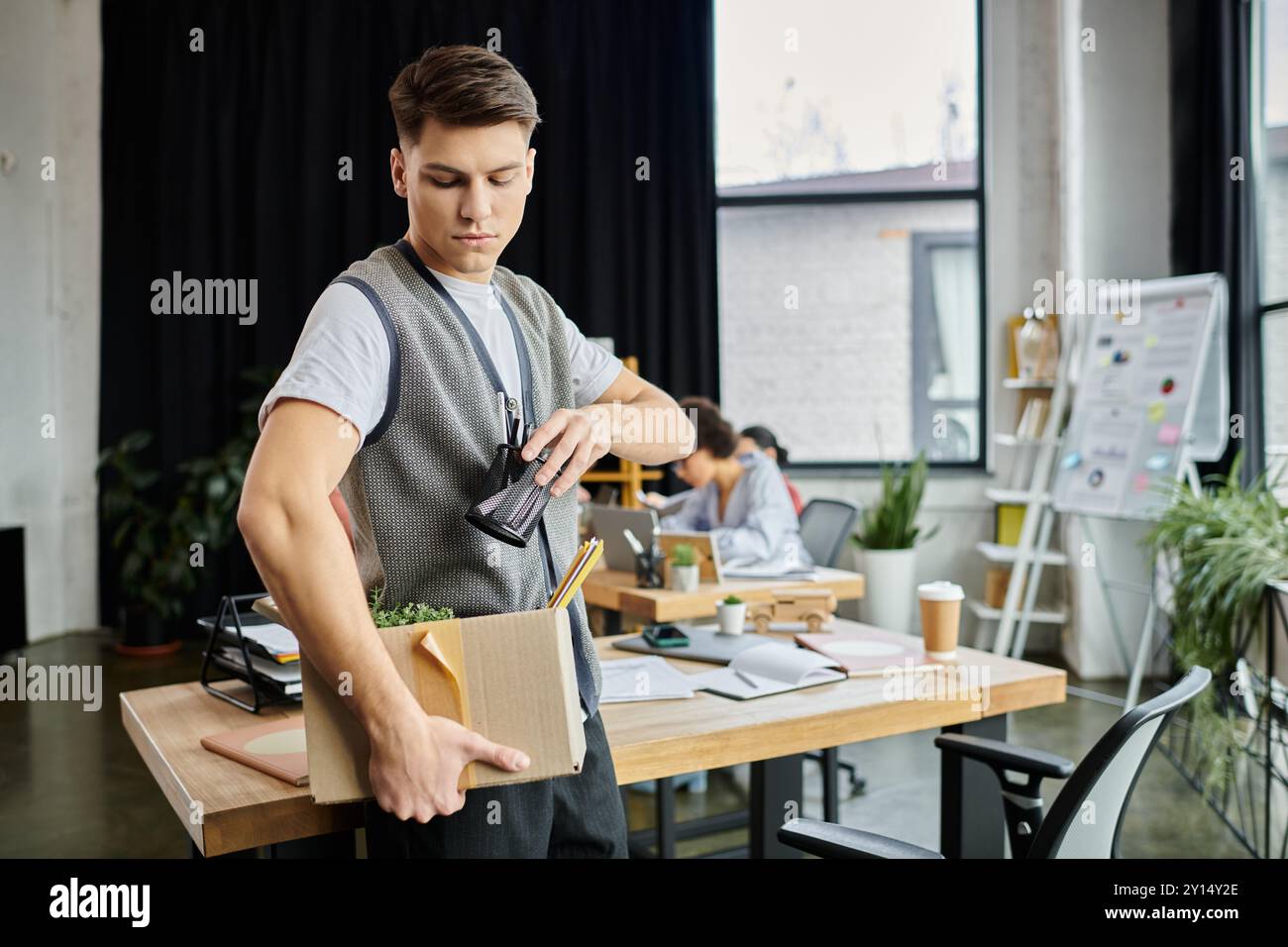 Young devoted man packing his items during lay off, colleagues on ...