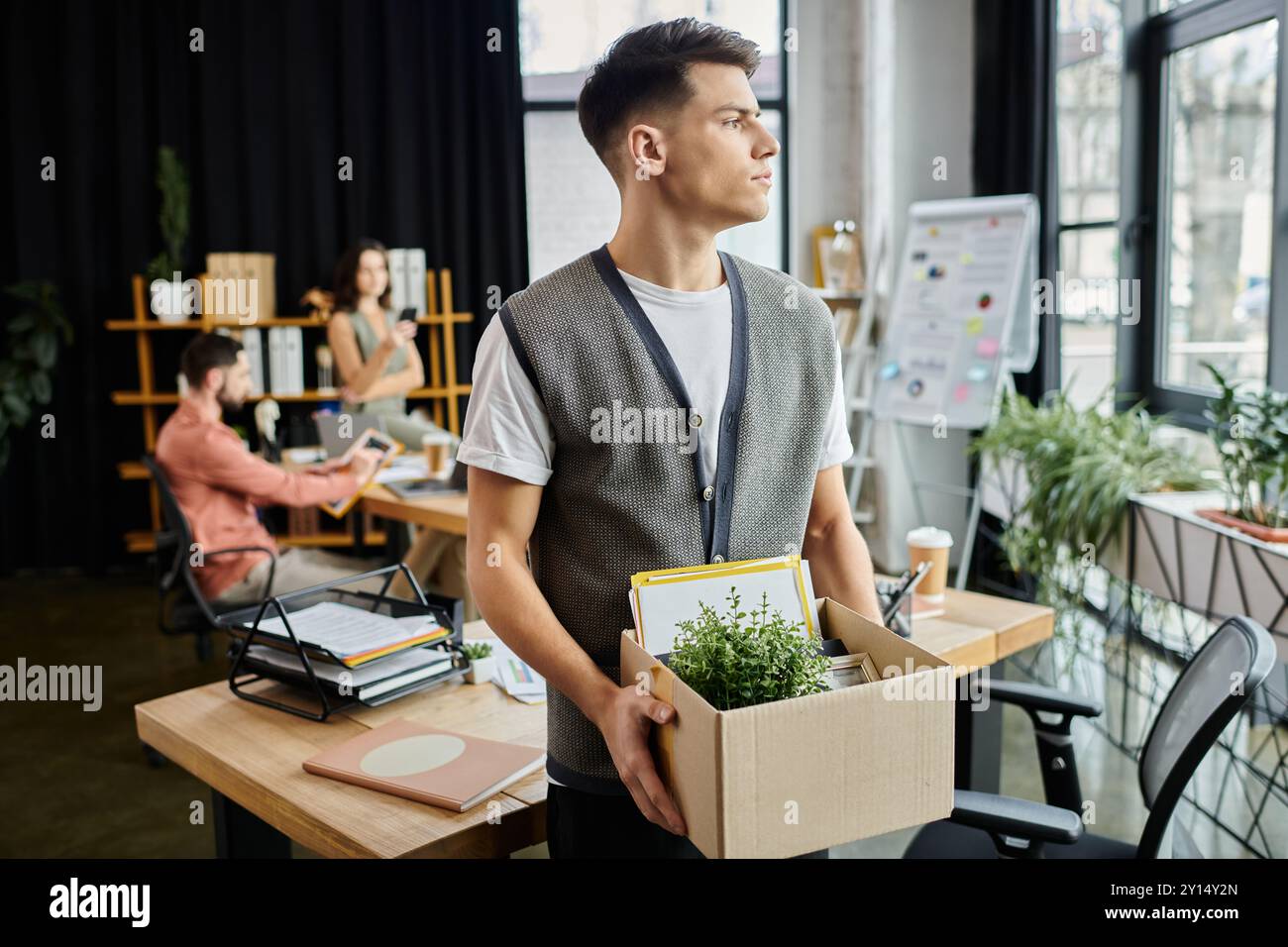 Young pensive man packing his items during lay off, colleagues on ...