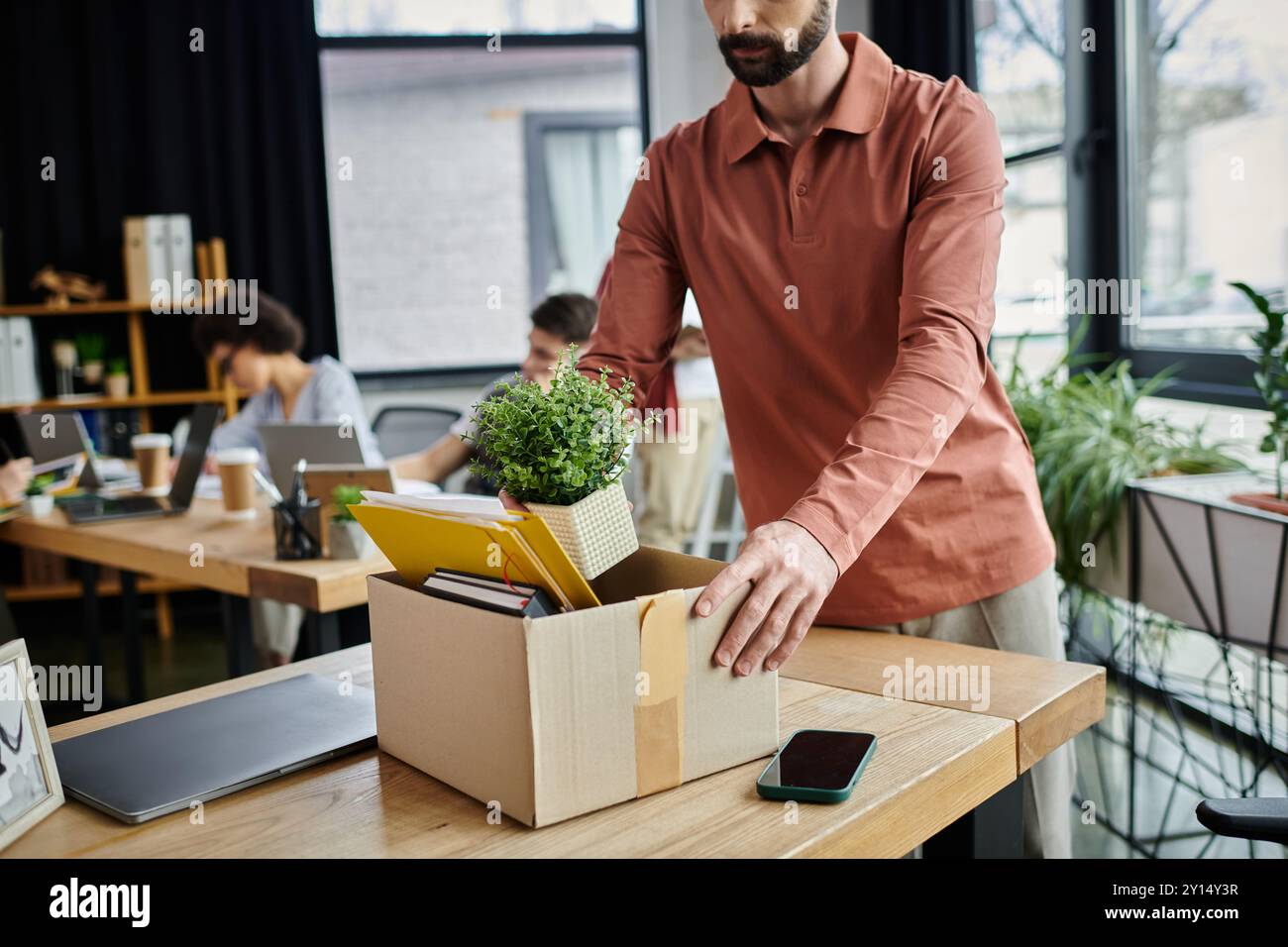 Dapper man packing his items during lay off, colleagues on backdrop ...