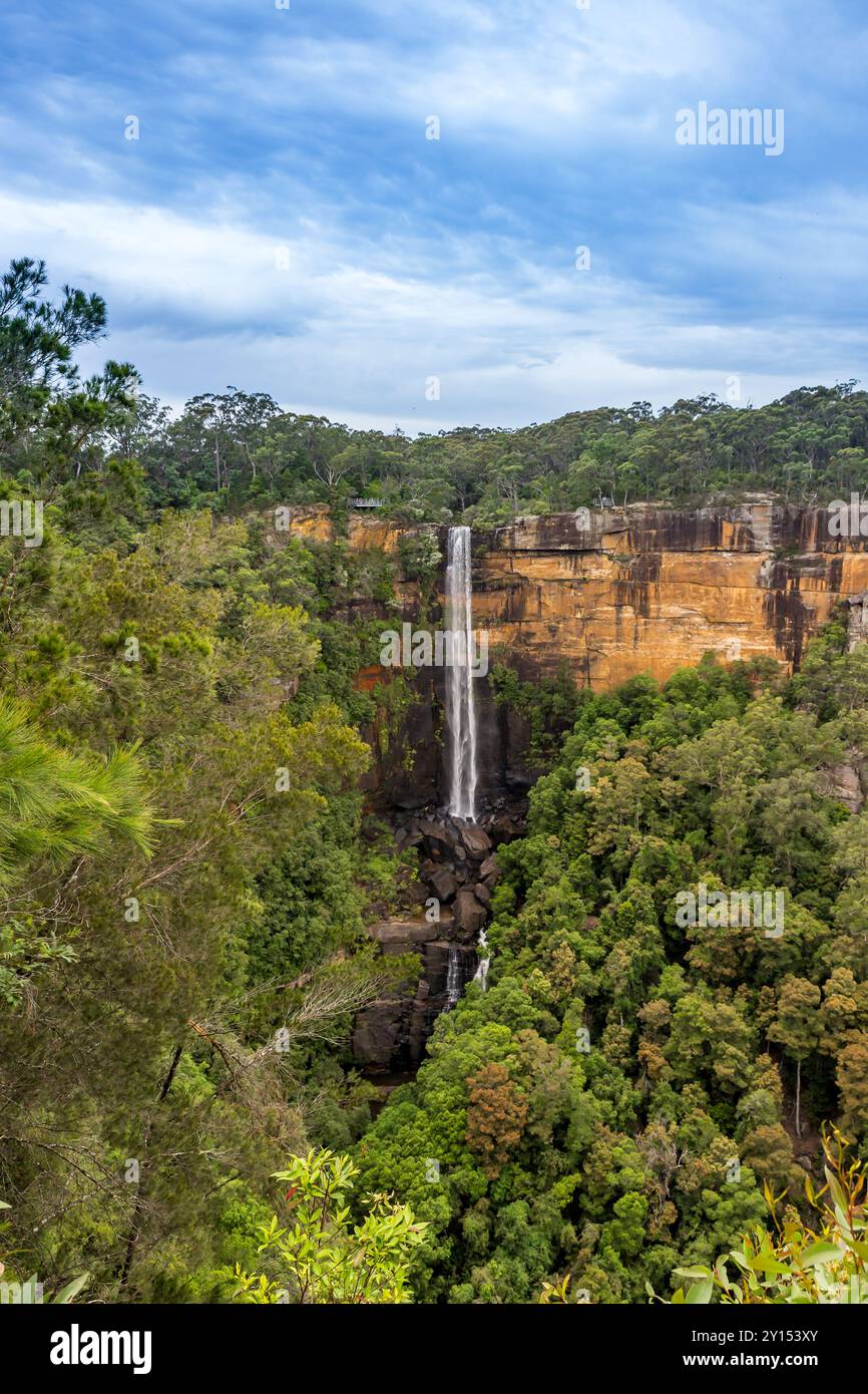 A tall waterfall flows smoothly over rugged cliffs, creating a ...