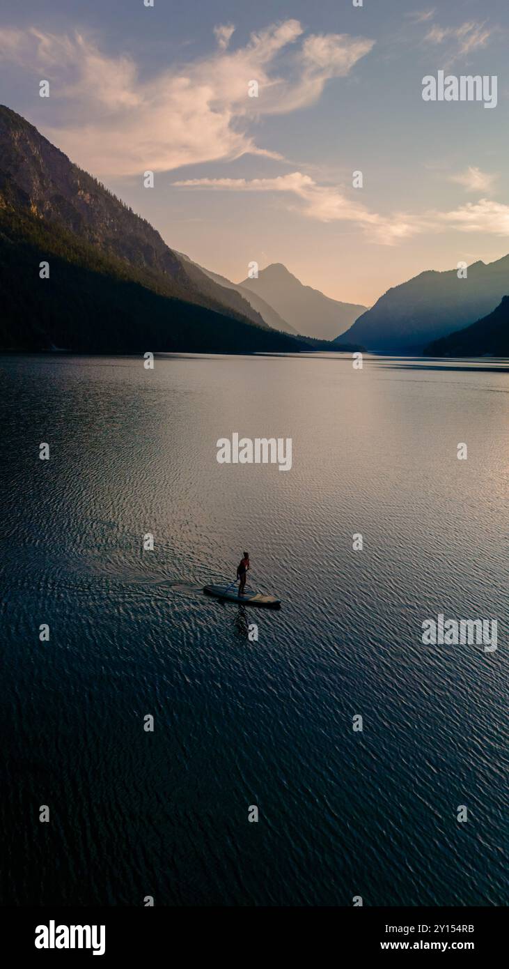 A lone paddler glides across the tranquil waters of Lake Plansee as the ...
