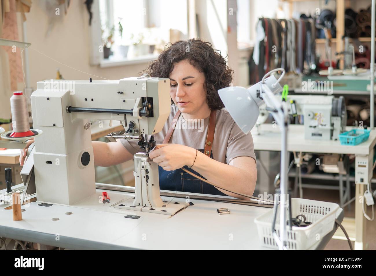 A woman tanner sews a leather belt on a sewing machine Stock Photo - Alamy