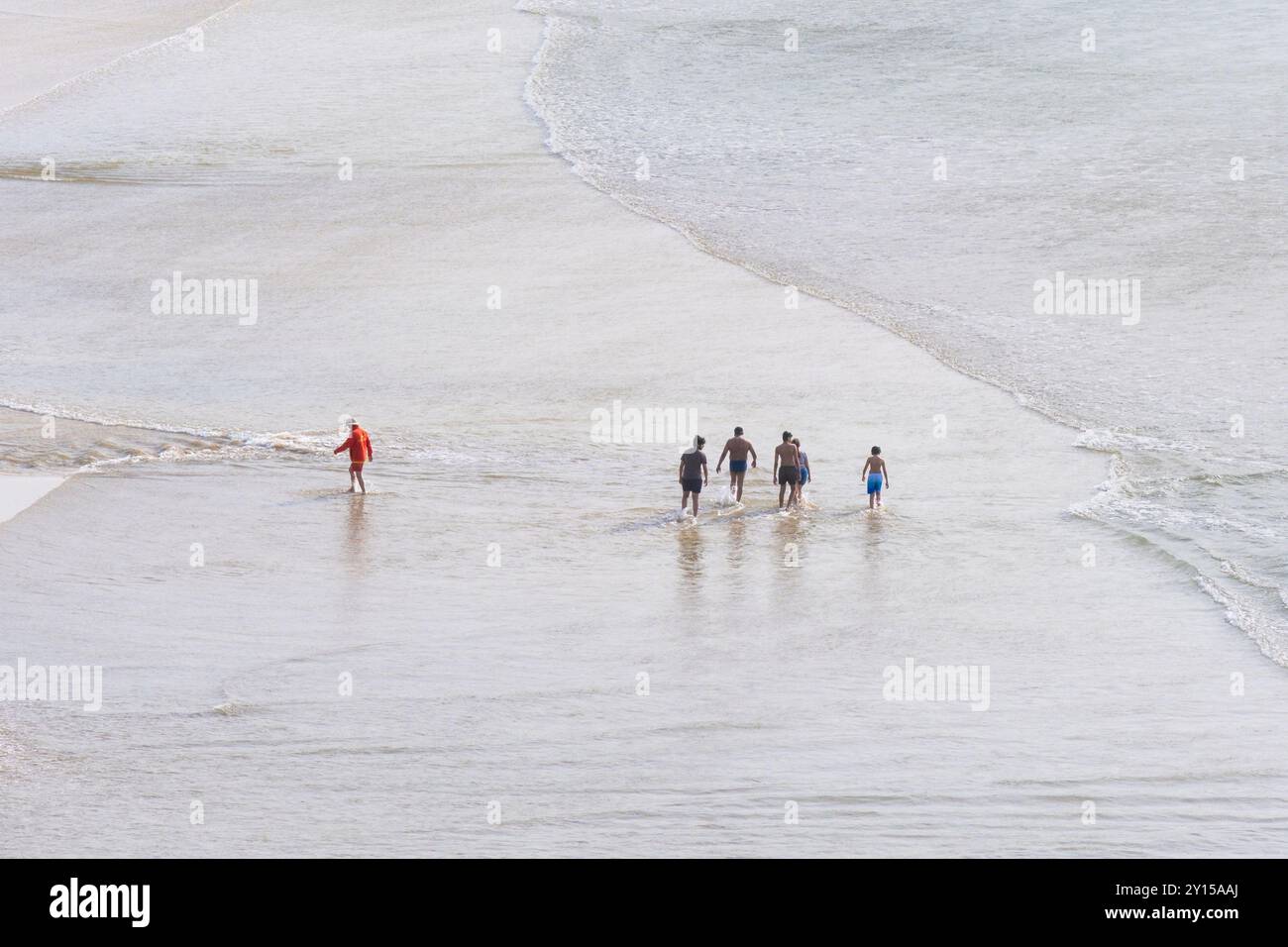 A RNLI Lifeguard walking away from a group of holidaymakers on Crantock ...
