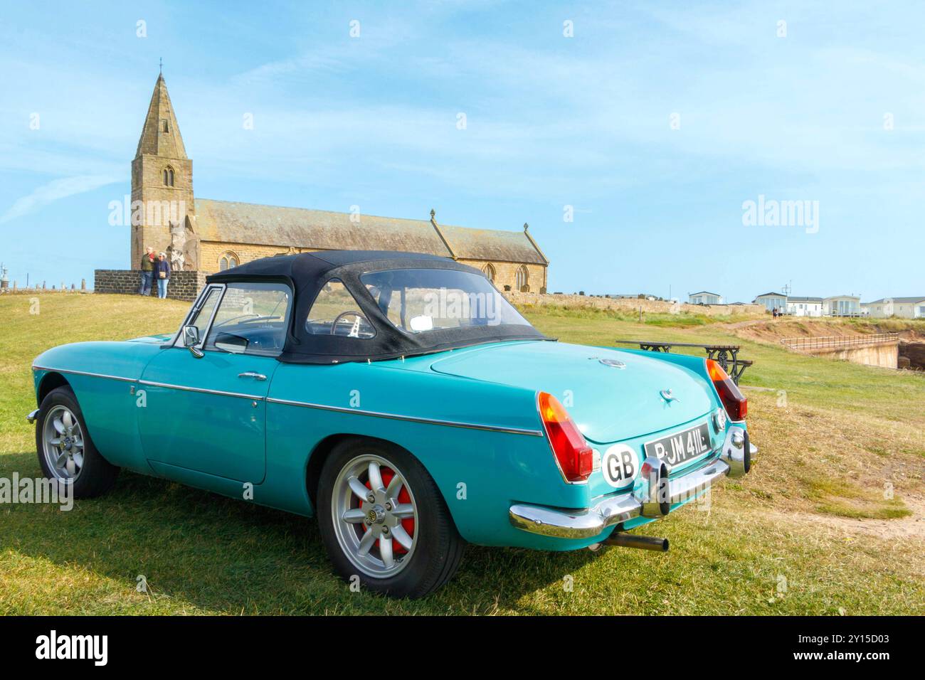 A vintage blue MG midget convertible car is parked on a grassy area ...
