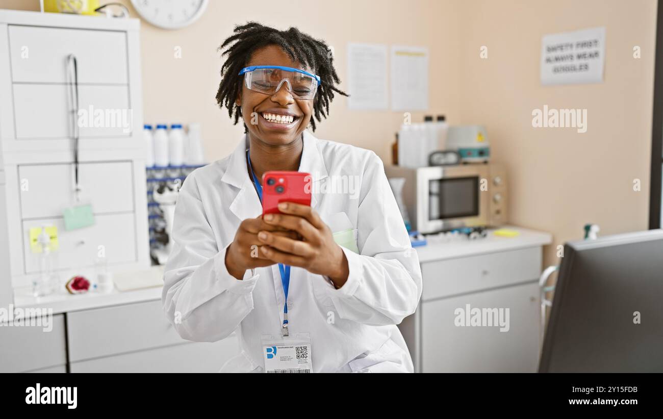 A cheerful woman scientist with dreadlocks using a smartphone in a lab ...