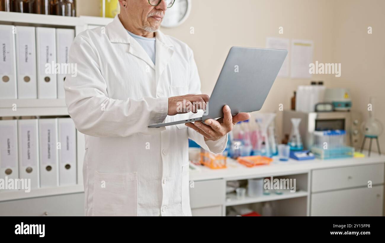 Grey-haired man in lab coat concentrating on a tablet in a modern ...