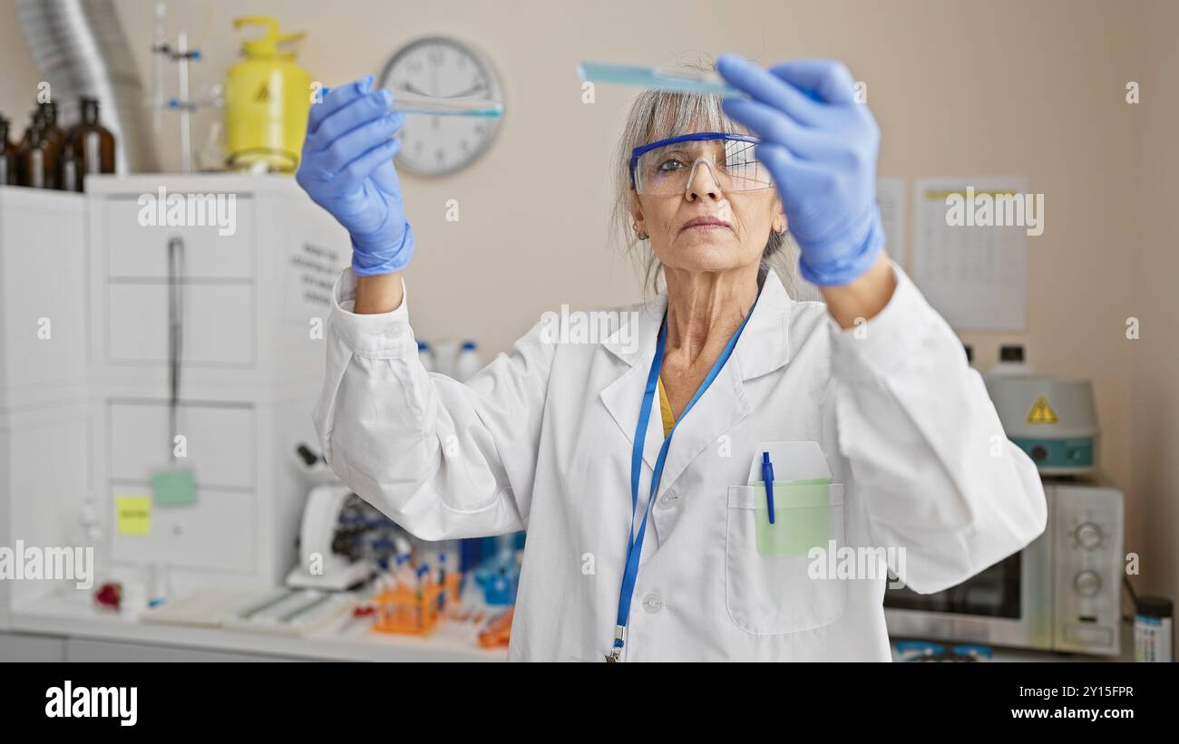 Mature woman scientist with grey hair examining a test tube in a ...